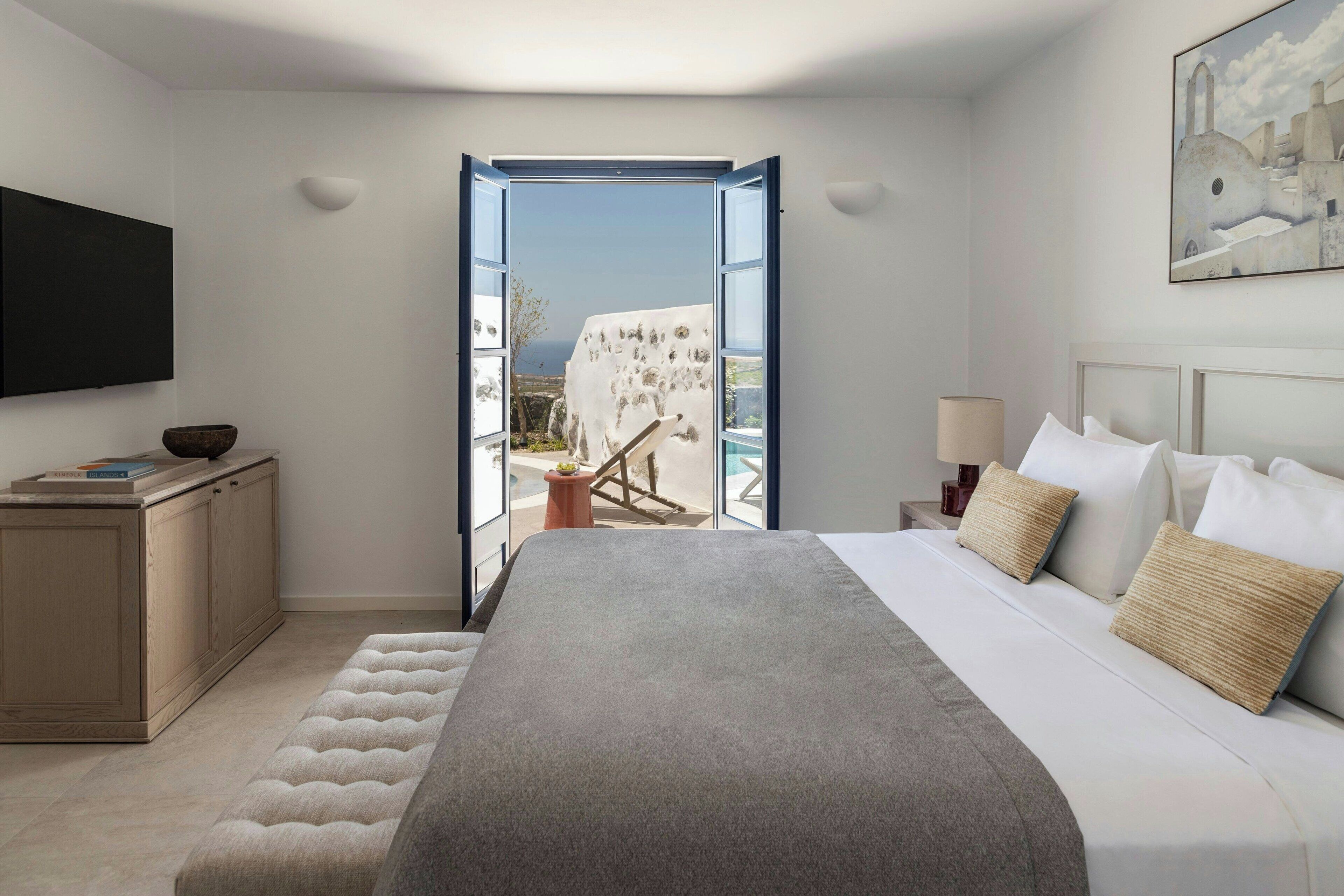 Quarto com cama grande, mesa de cabeceira, televisão na parede e vista para o exterior.
