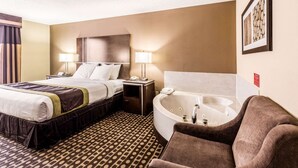 Quarto de hotel com uma cama, um espaço de estar com uma poltrona, uma banheira grande e uma mesinha de cabeceira com abajur.