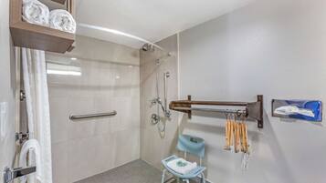 Uma casa de banho moderna com chuveiro, porta-toalhas, sanita e uma cadeira pequena.