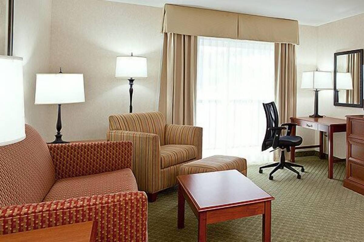 Quarto de hotel com sofá, poltrona, escrivaninha, televisão e uma cama.