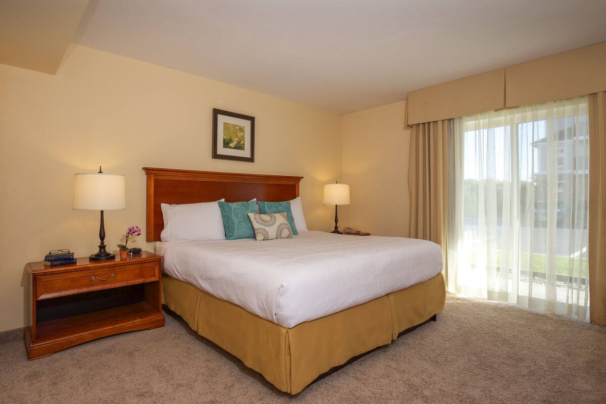 Quarto de hotel com uma cama grande, duas mesas de cabeceira e uma janela com cortinas.