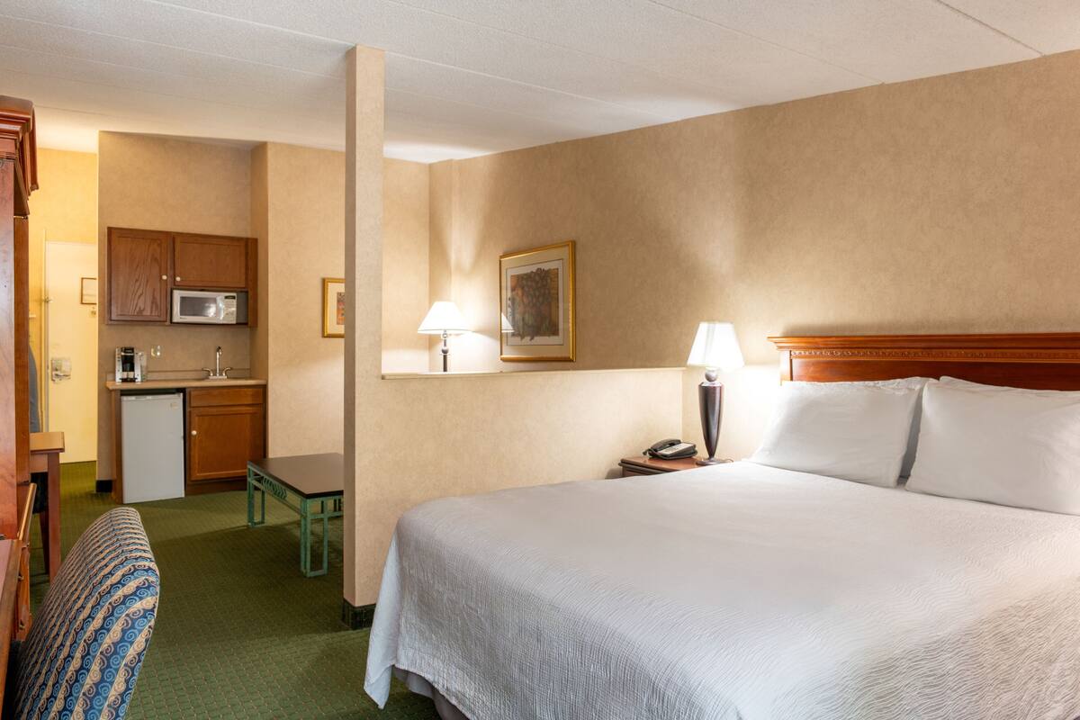 Quarto de hotel com cama, escrivaninha, cadeira, micro-ondas e uma pequena cozinha.