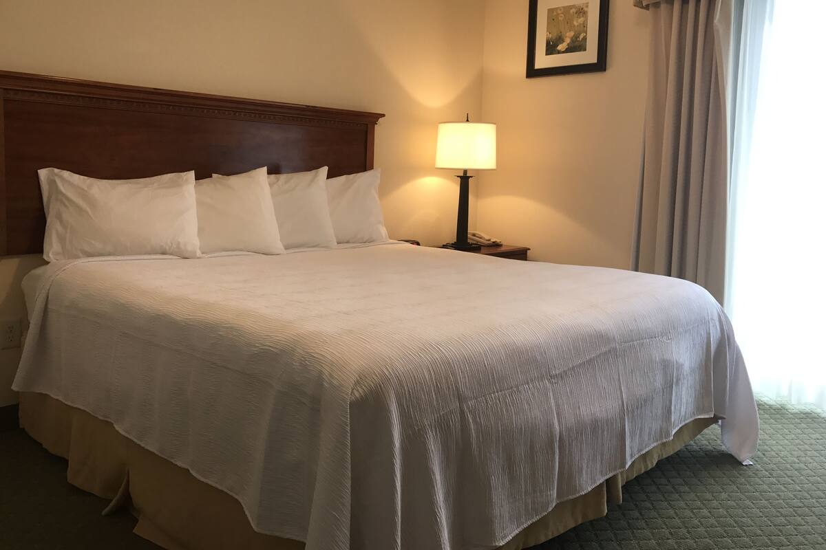 Cama bem arrumada com cabeceira de madeira, abajur e um quadro na parede.