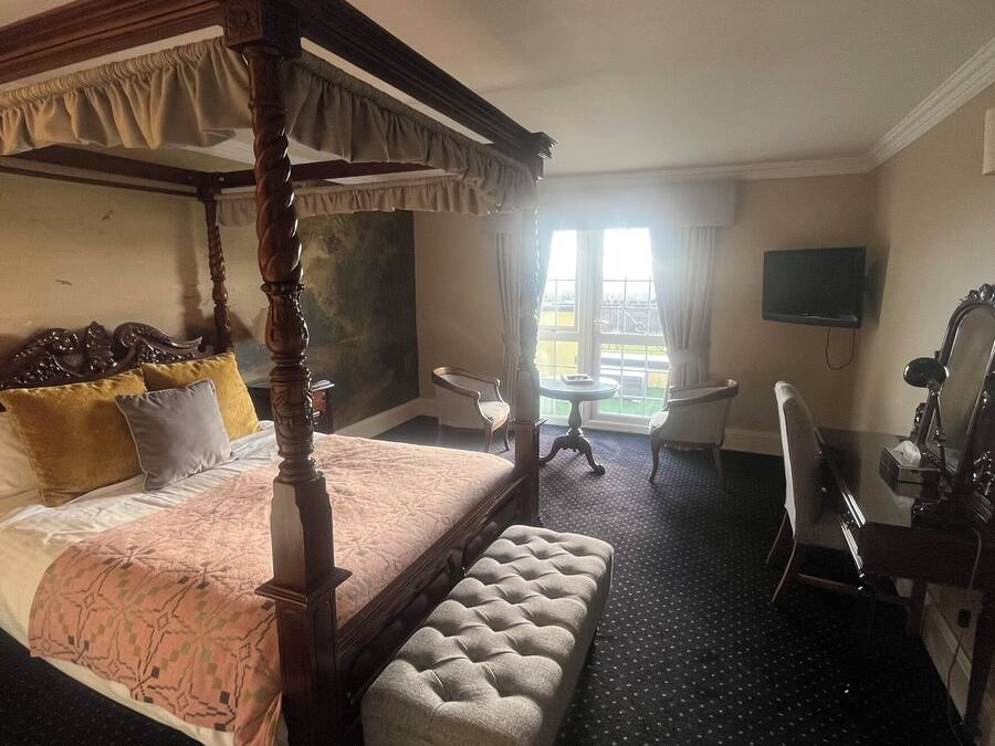 Uma cama com dossel, um banco, uma escrivaninha, uma cadeira e uma TV em um quarto de hotel.