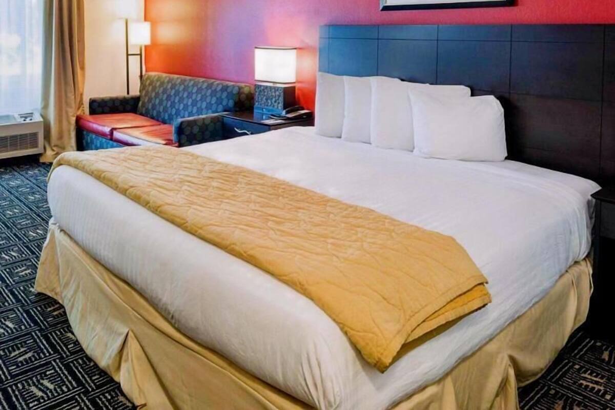 Quarto de hotel com uma cama grande, escrivaninha, cadeira e janela com cortinas.