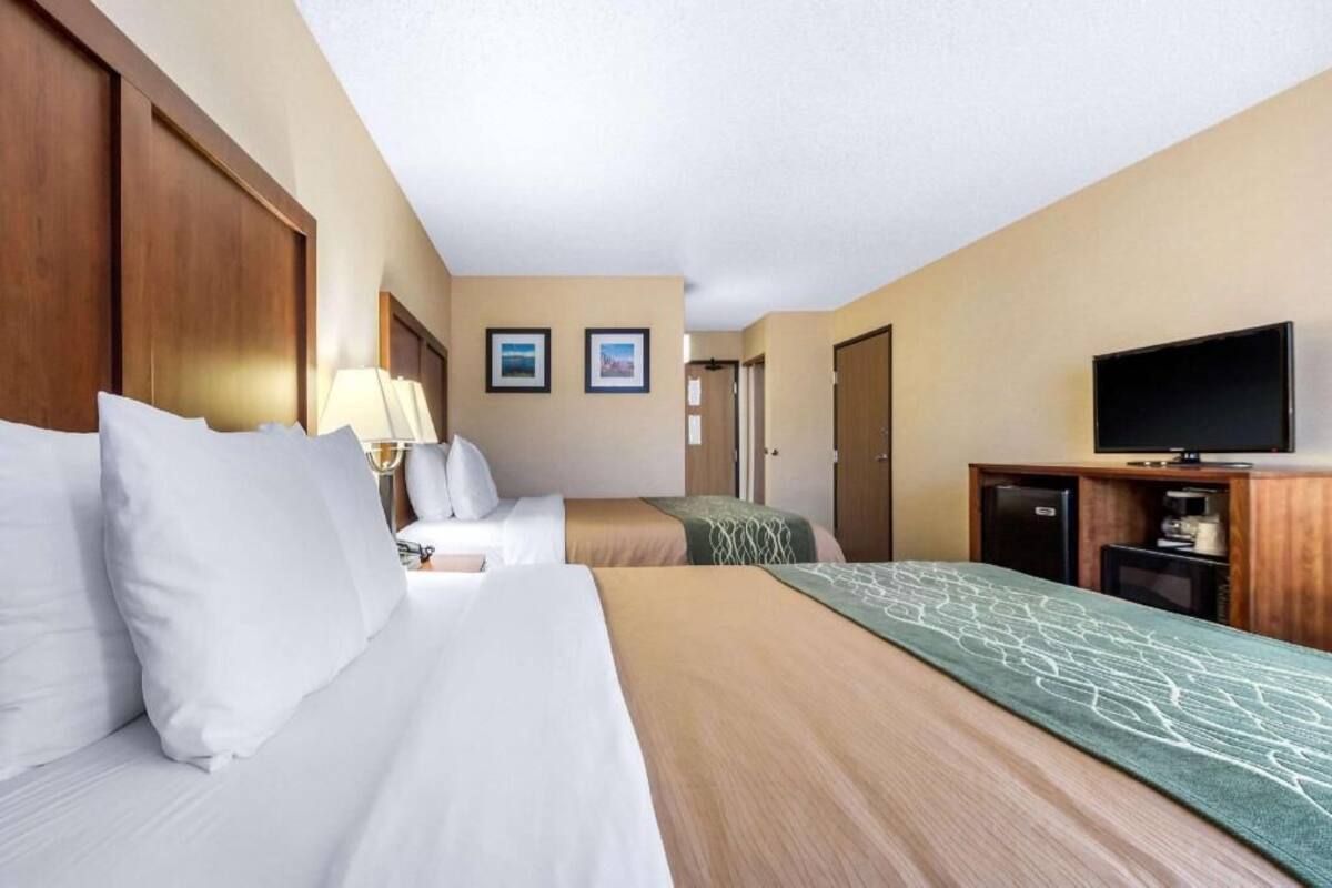 Quarto de hotel com duas camas, televisão, escrivaninha e computador, além de uma porta.