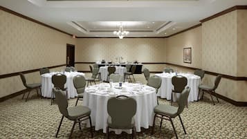 Sala de conferências com várias mesas redondas, cada uma com toalhas brancas, cadeiras e utensílios para refeições.