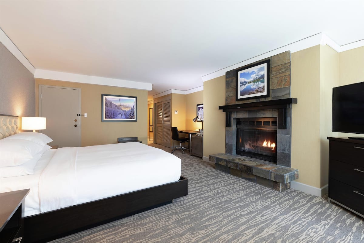 Quarto de hotel com uma cama grande, lareira, escrivaninha e televisão.