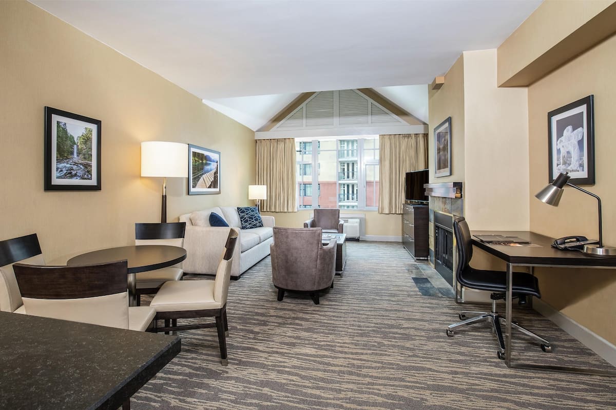 Quarto de hotel com sofá, poltronas, escrivaninha e mesa de jantar.