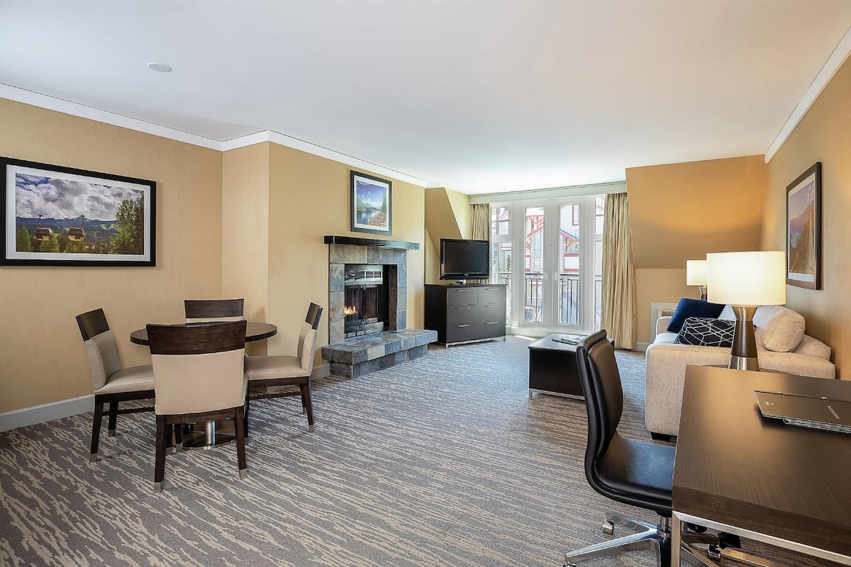 Quarto de hotel com lareira, televisão, área de jantar com cadeiras, sofá e escrivaninha com abajur.