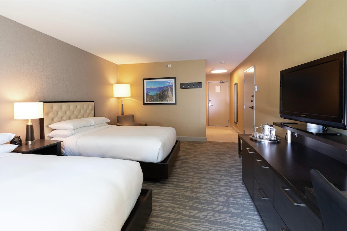 Quarto de hotel com duas camas, televisão, escrivaninha com abajur e um quadro na parede.