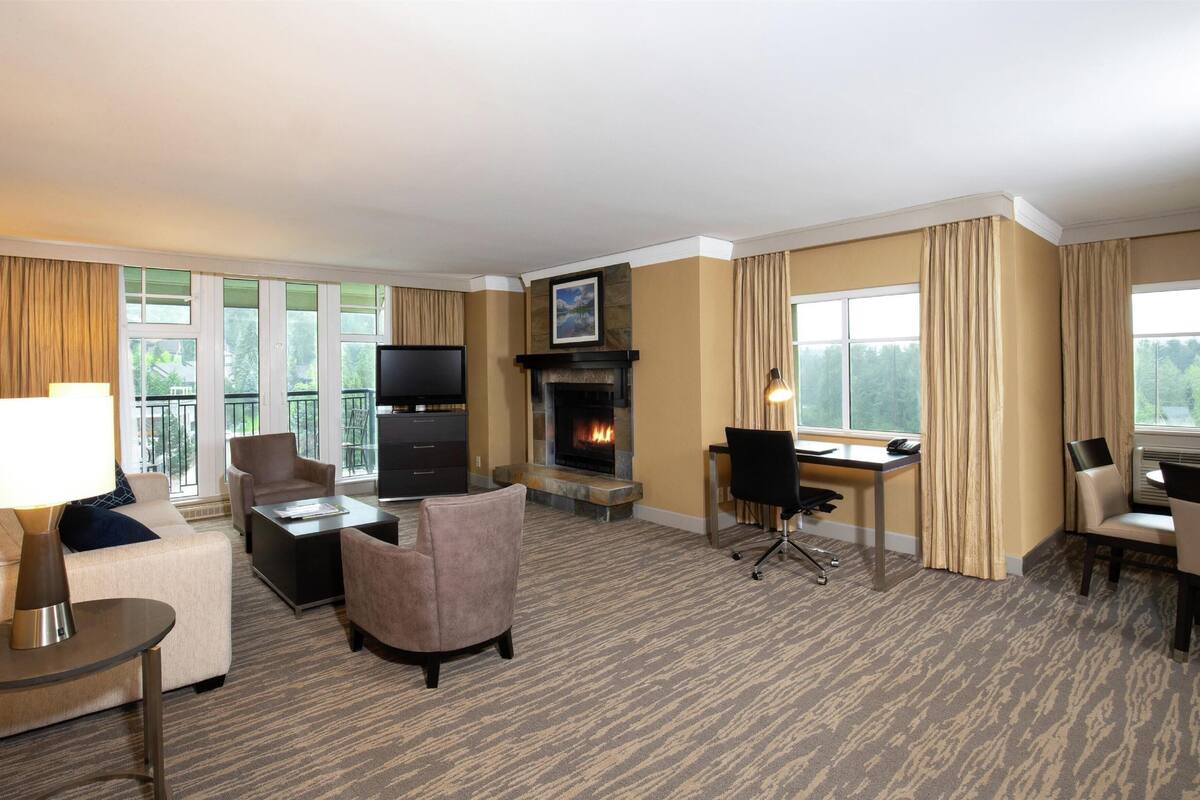 Quarto de hotel com lareira, televisão, escrivaninha e varanda com cortinas.