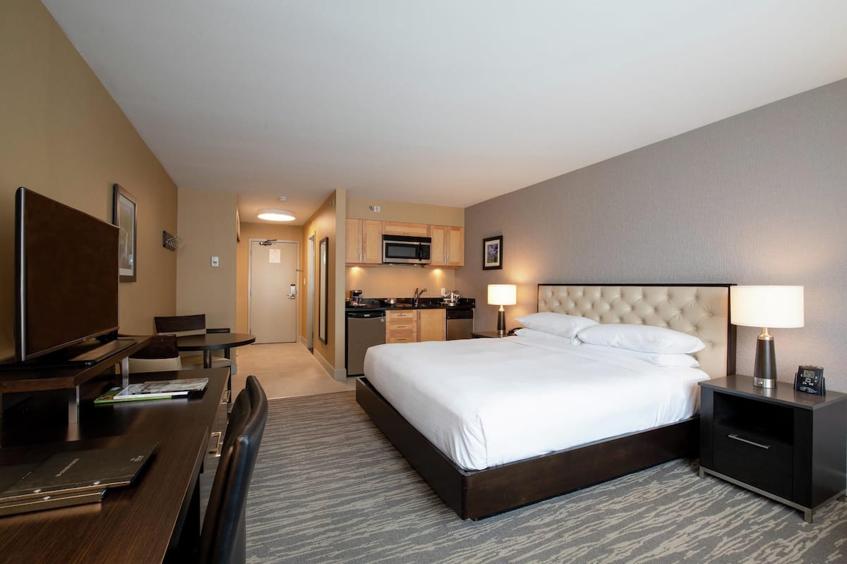 Quarto de hotel com uma cama grande, uma escrivaninha com cadeira, televisão, micro-ondas e uma pequena copa.