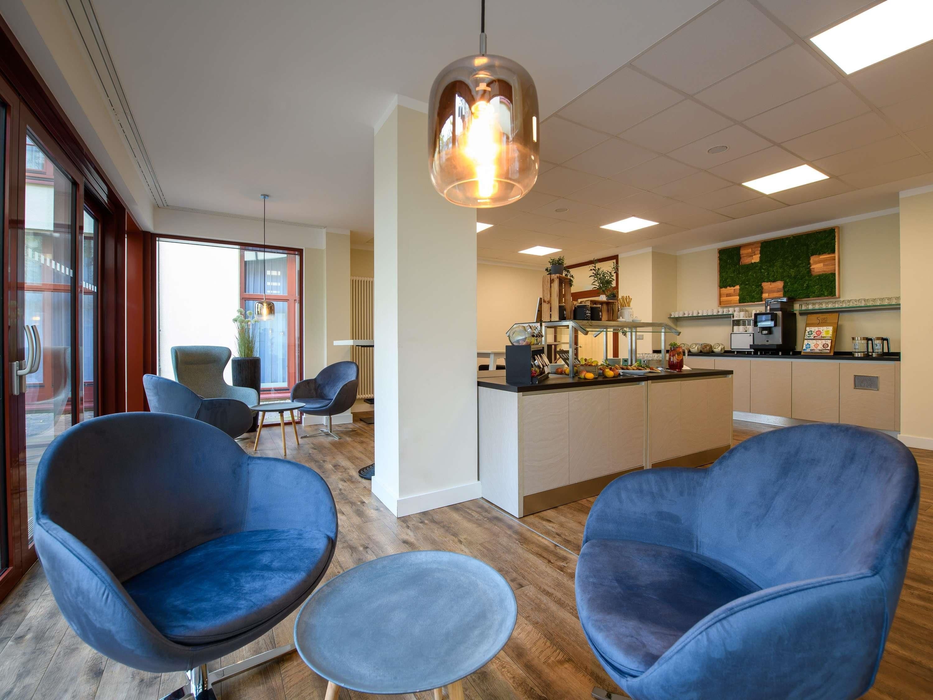 Interior moderno com duas poltronas azuis, uma mesa redonda pequena, um espaço para café e vista através de uma porta de vidro.