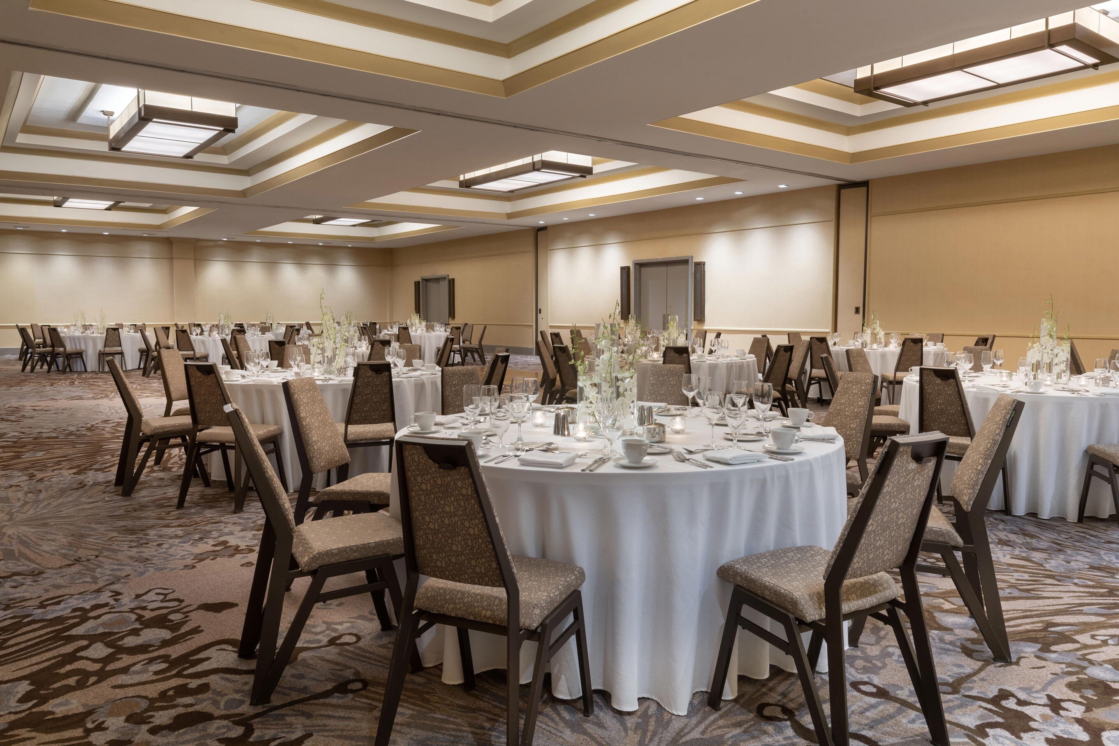 Uma sala de conferências ampla, com mesas redondas dispostas para refeições, equipada com cadeiras e louças.