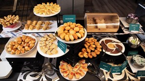 Uma mesa de buffet com diversos alimentos, incluindo pão, pastelaria e sobremesas.