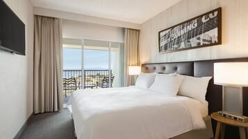 Quarto de hotel com cama, duas luminárias, televisão, janela com cortinas e um quadro na parede.