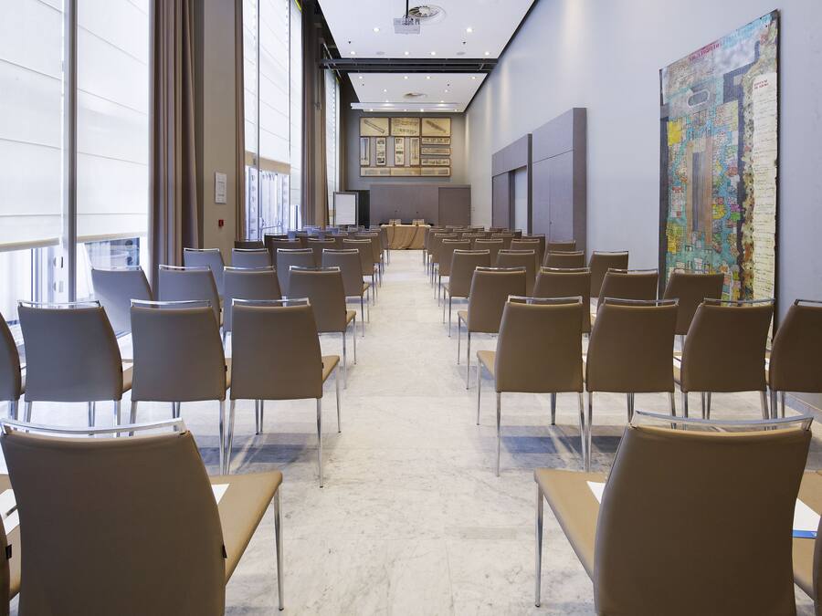 Uma sala de conferências com fileiras de cadeiras, um vão de janela grande e um mapa na parede.