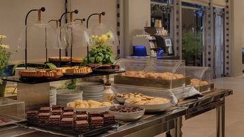 Buffet com diversos produtos de pastelaria e sobremesas, incluindo bolos e doces, expostos em cúpulas de vidro.