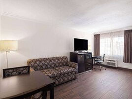 Quarto de hotel com sofá, televisão, escrivaninha e cadeira.