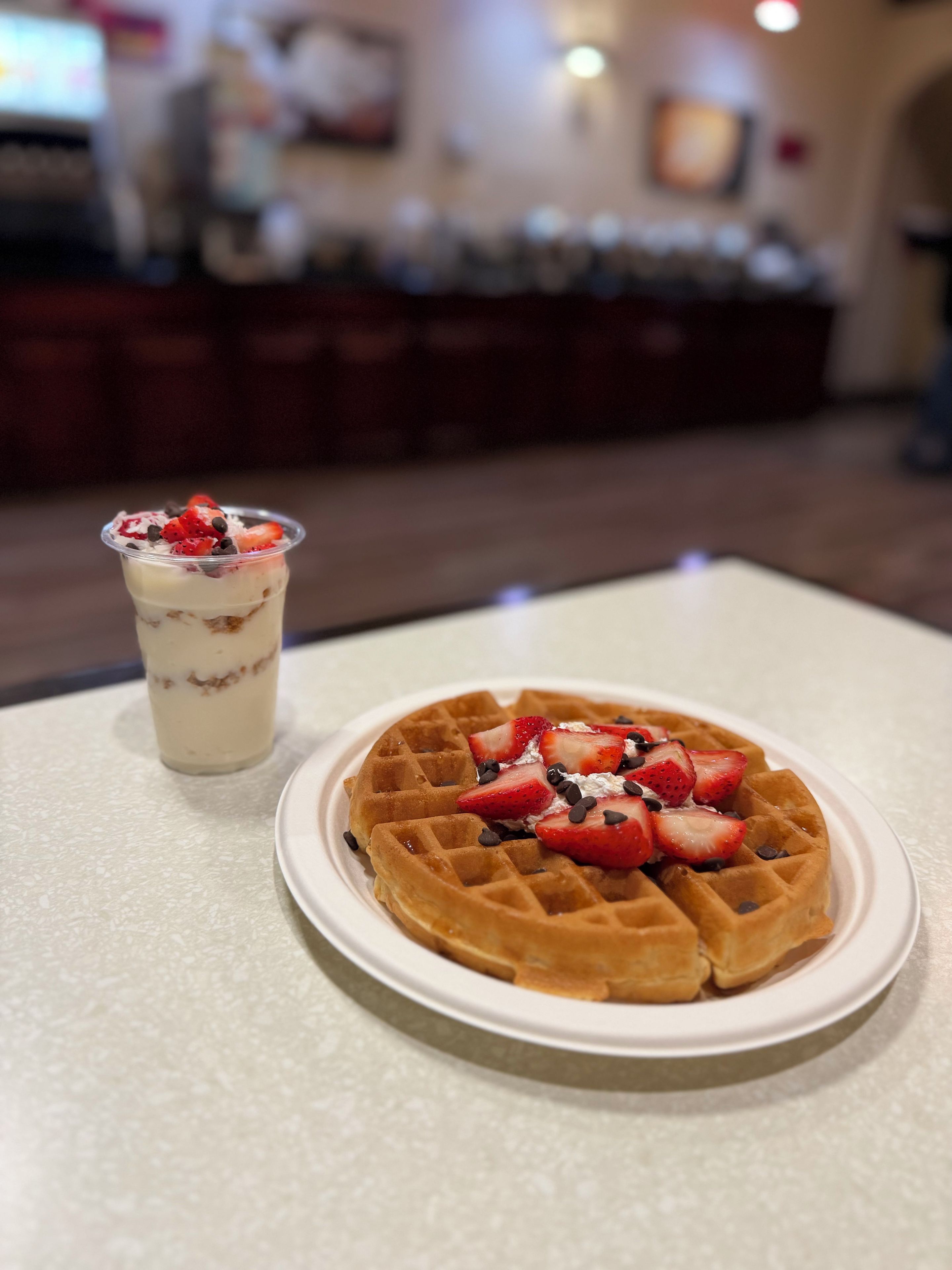 Waffle coberto com morangos e gotas de chocolate, e sobremesa em camadas servida em copo.