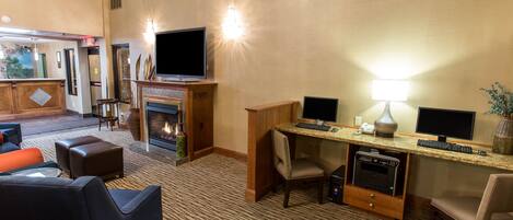 Um hall de hotel com lareira, área de estar e balcão com computadores.