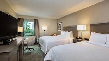 Quarto de hotel com duas camas, uma mesa de trabalho, uma televisão, uma cadeira e uma janela com cortinas.