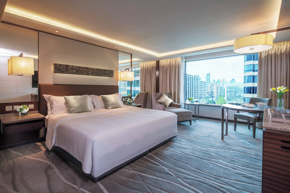 Quarto de hotel com uma cama grande, uma escrivaninha e vista para a cidade.