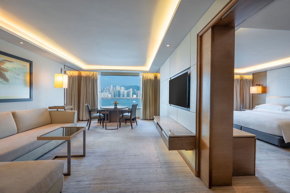 Quarto de hotel moderno com vista para a cidade, televisão de tela plana, sofá, mesa de jantar e uma cama.