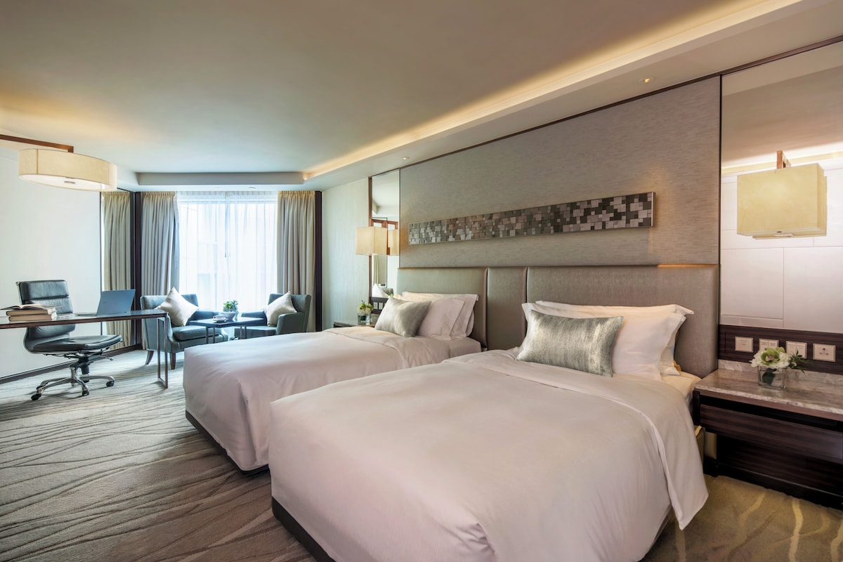 Quarto de hotel com duas camas, uma escrivaninha e uma cadeira.
