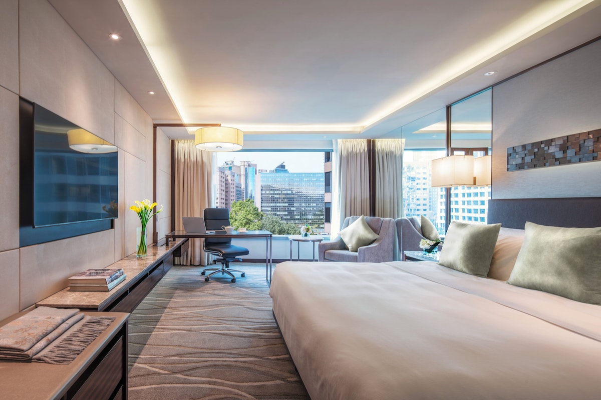 Quarto de hotel moderno com uma cama grande, uma mesa, uma cadeira e uma TV fixada na parede.
