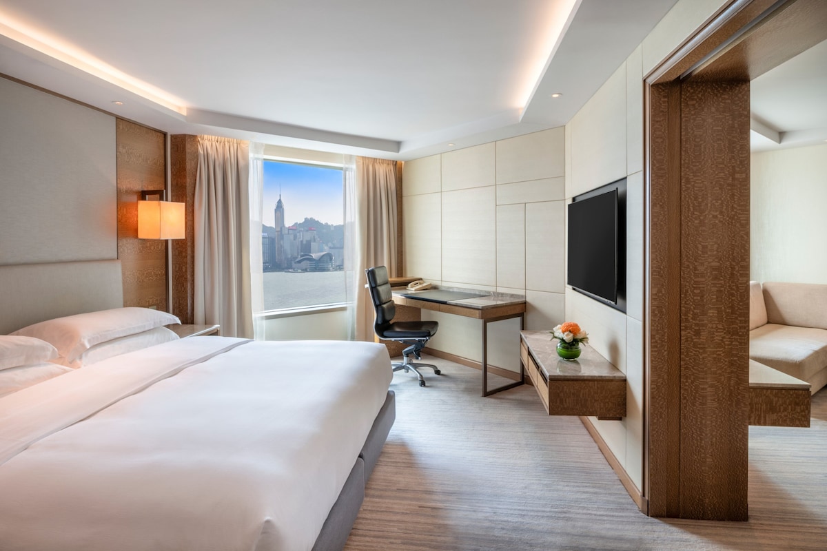 Quarto de hotel com uma cama grande, uma escrivaninha com cadeira, televisão e vista para a cidade.