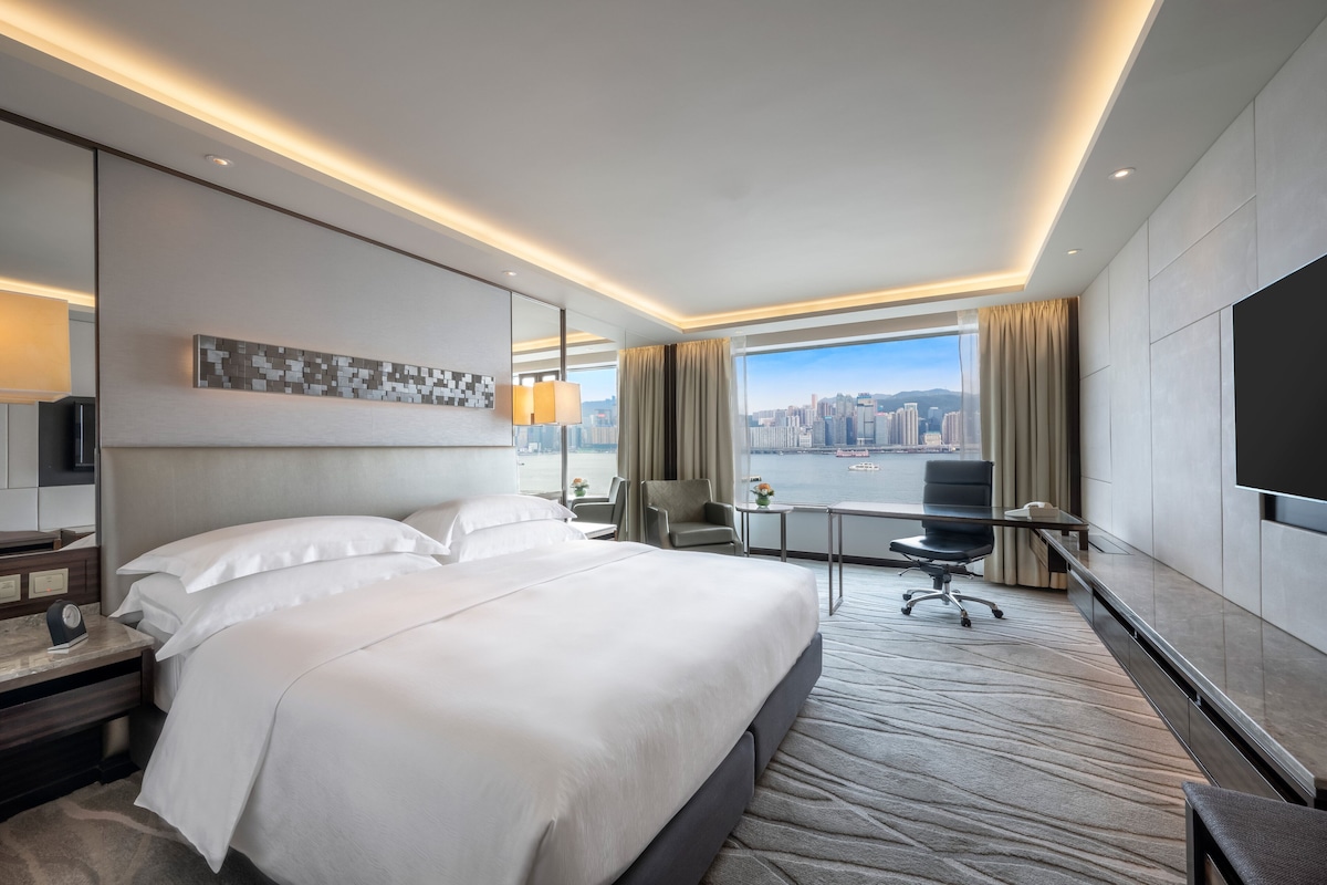 Quarto de hotel moderno com uma cama grande, uma escrivaninha, uma cadeira e uma televisão.