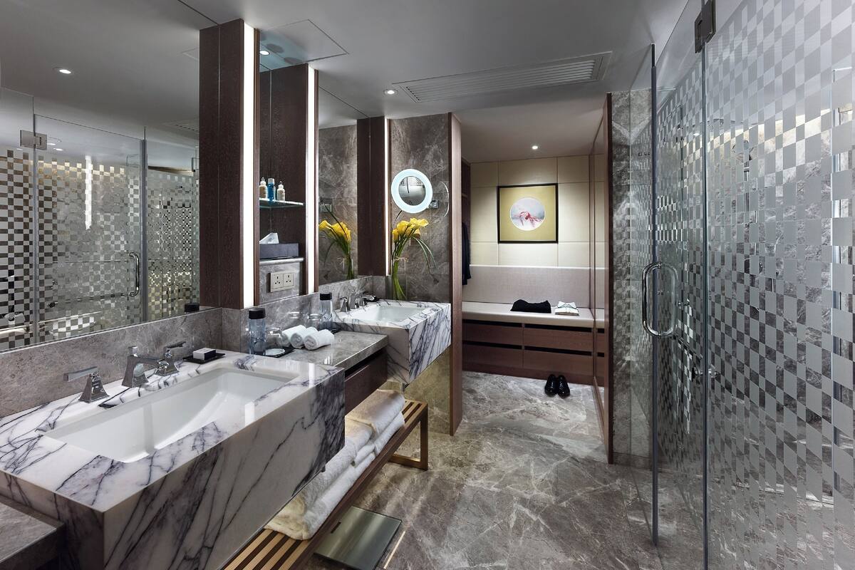 Um banheiro moderno com um amplo lavatório, várias pias, chuveiro sem barreiras e um espelho com moldura decorativa.