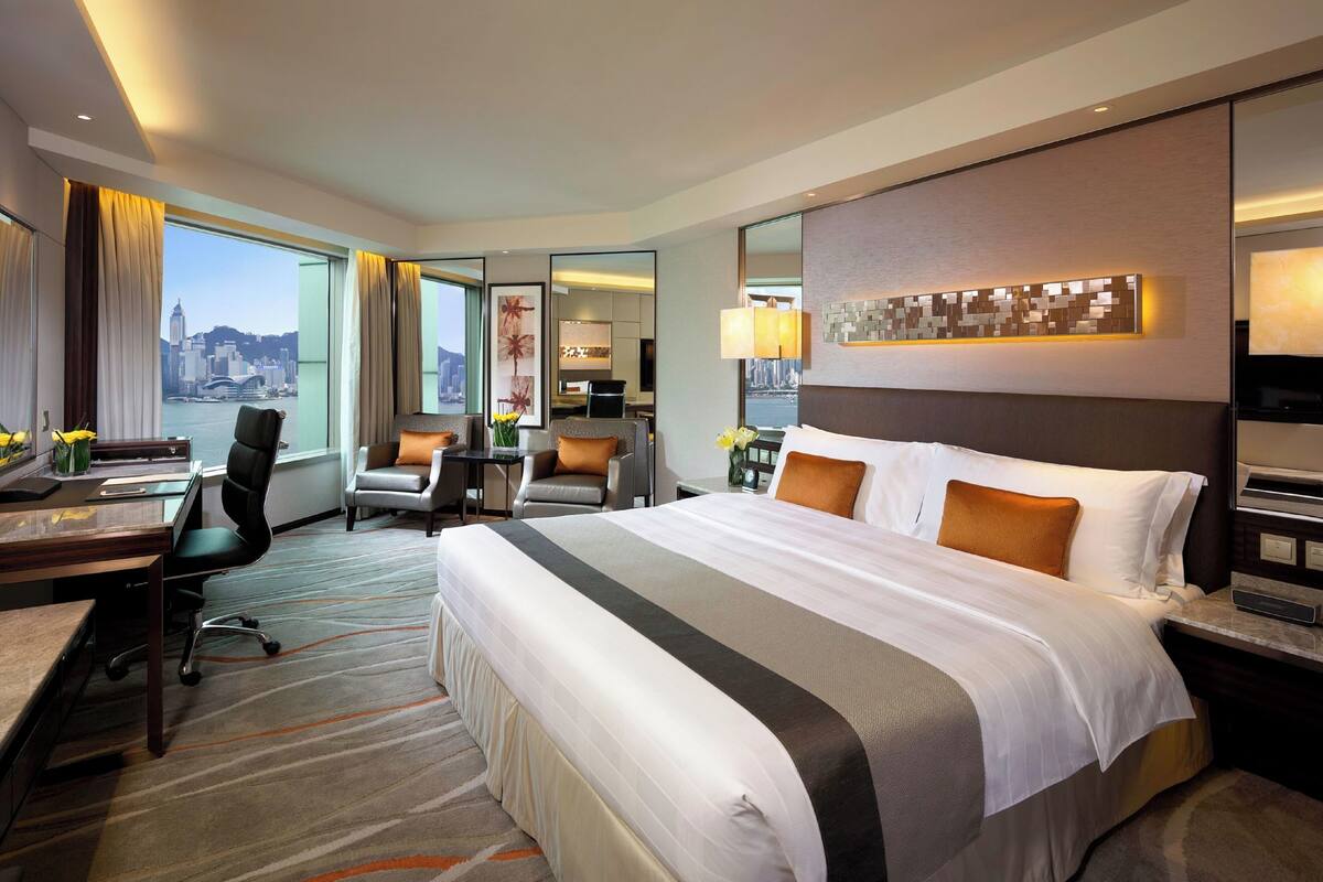 Quarto de hotel com uma cama grande, uma escrivaninha, uma cadeira, televisão e vista para a cidade.
