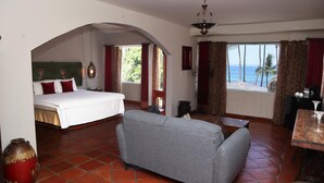 Quarto de hotel com cama, sofá, mesa de jantar e vista para o oceano.