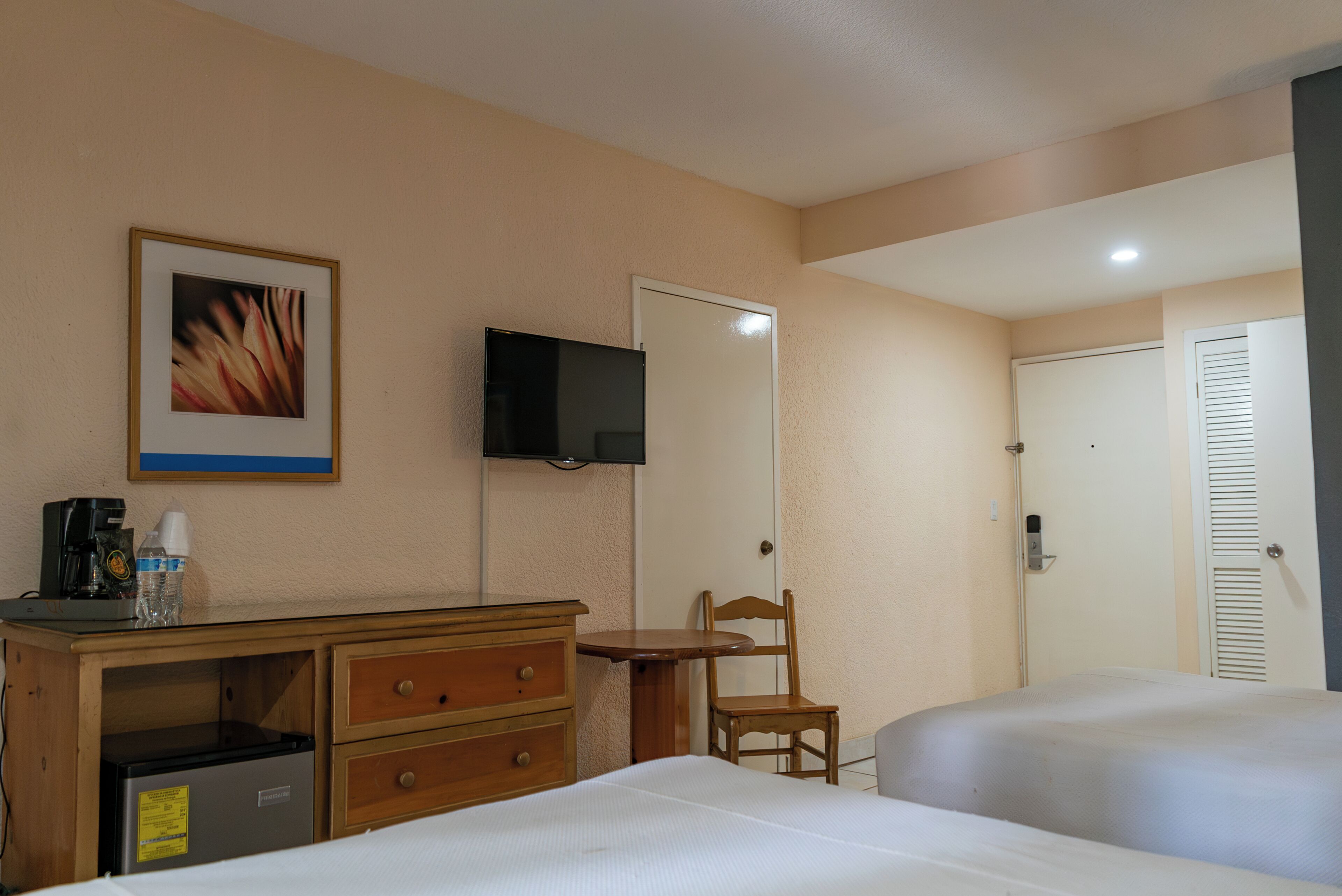 Quarto de hotel com cama, escrivaninha, cadeira, televisão, minibar e porta.