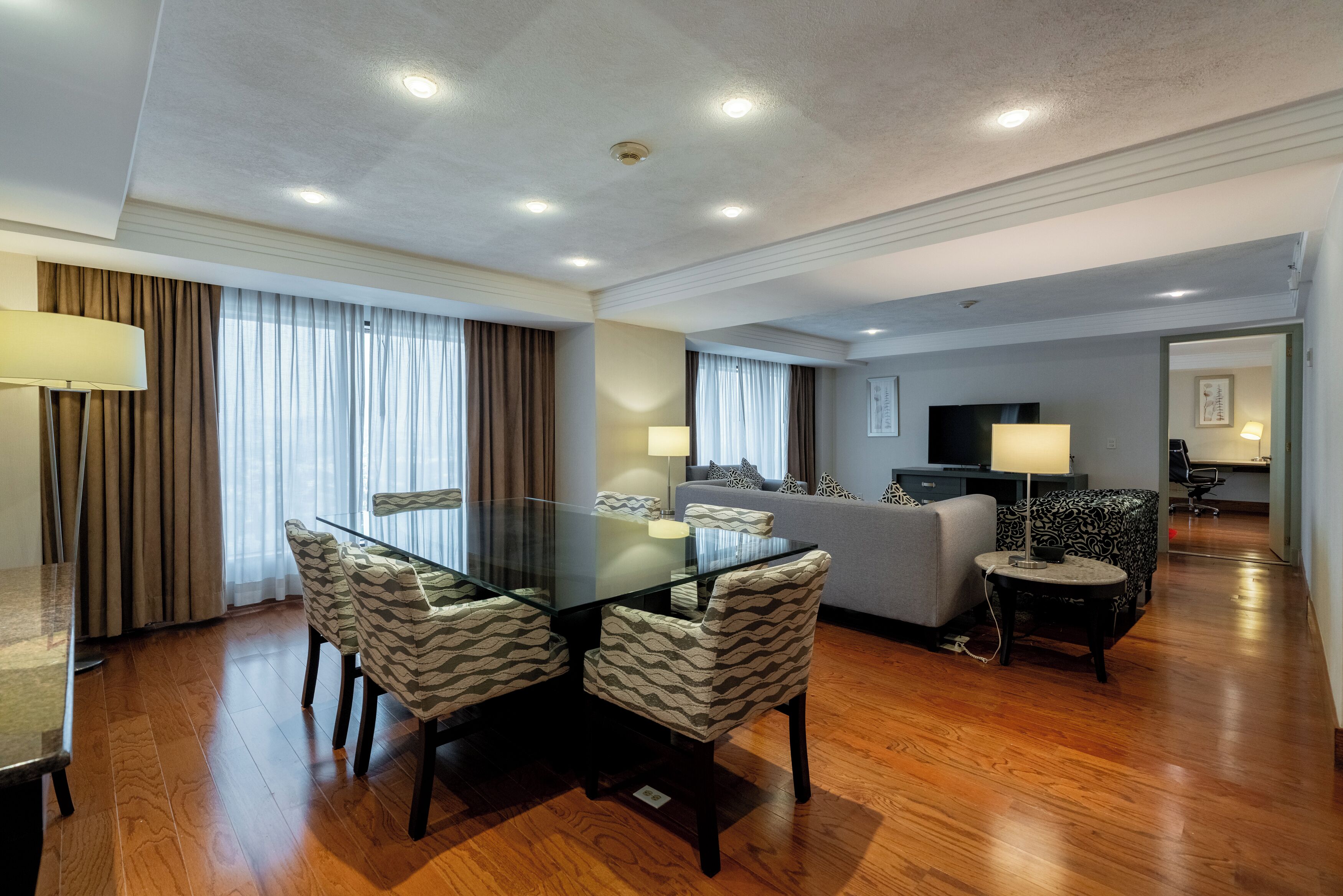 Quarto de hotel com uma mesa de jantar, cadeiras, um sofá, uma televisão e um abajur.