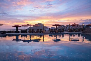 Área de piscina com guarda-sóis e espreguiçadeiras, refletindo o céu do pôr do sol.