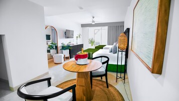 Quarto de hotel moderno com área de refeições, uma cama com roupa de cama verde, um ventilador de teto e uma janela grande com cortinas.
