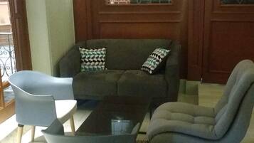 Uma sala de estar com um sofá cinzento, duas poltronas, uma mesa de centro e pisos com azulejos estampados.