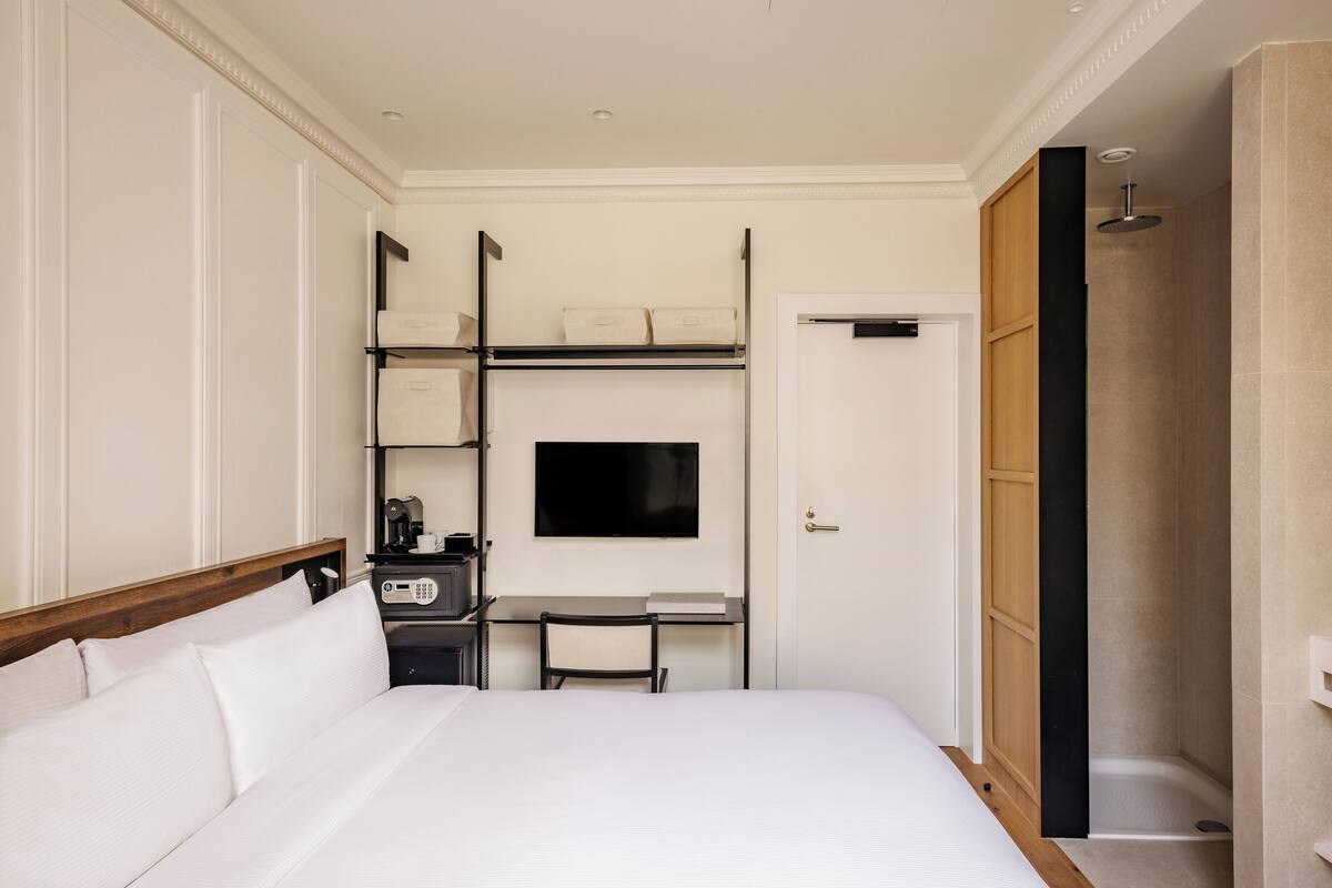 Quarto de hotel com cama, escrivaninha, televisão e chuveiro.