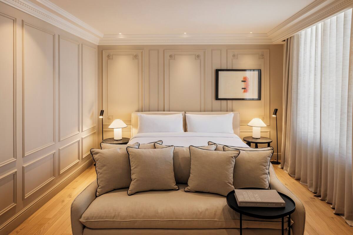 Quarto de hotel com uma cama grande, duas mesas de cabeceira com luminárias, um sofá e um quadro na parede.