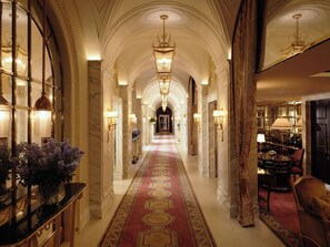 Um amplo corredor de hotel com paredes de mármore, lustres e tapete vermelho.