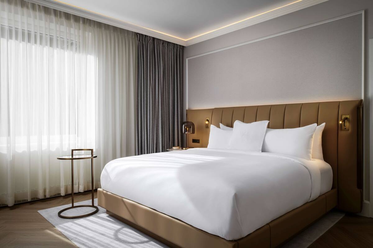Quarto de hotel moderno com uma cama grande, uma mesa de cabeceira e uma luminária.