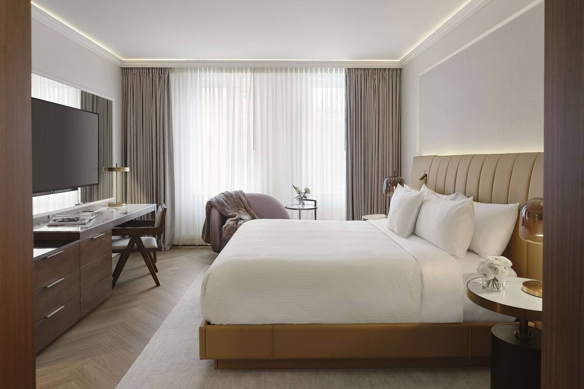 Quarto de hotel com uma cama, uma escrivaninha, uma TV e uma mesinha de cabeceira com abajur.