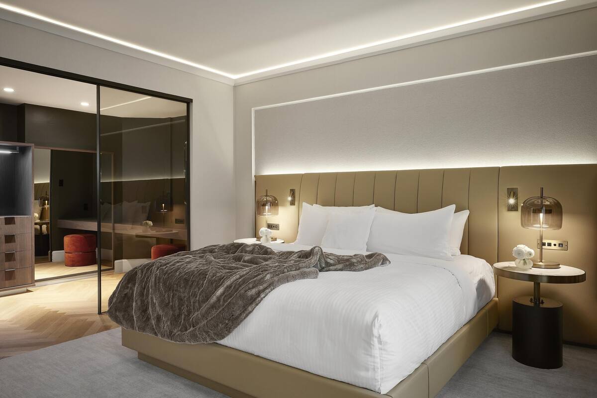 Quarto moderno com uma cama grande, mesas de cabeceira, divisória de vidro e guarda-roupa de madeira.