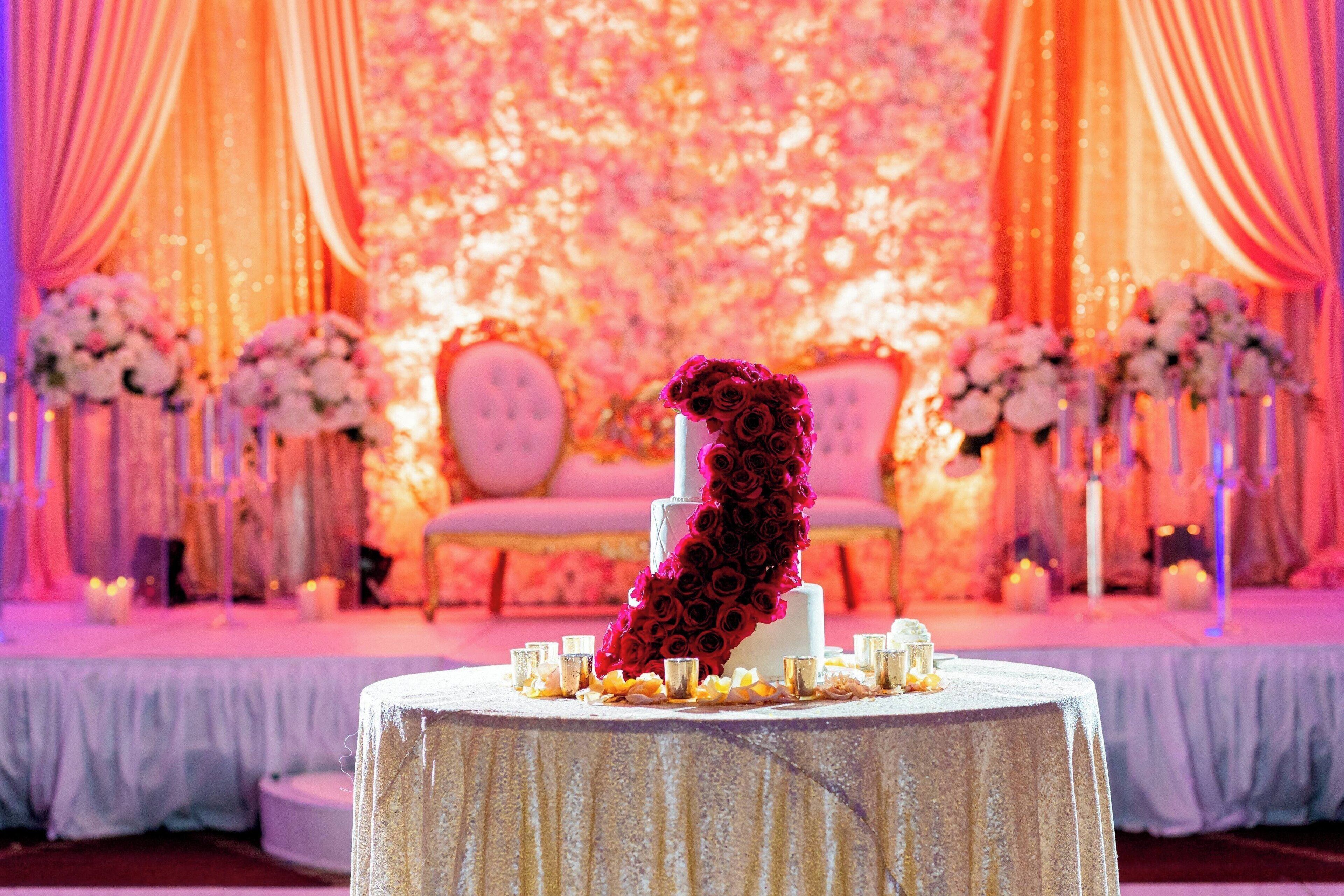 Palco de casamento com bolo de andares, arranjos florais e cortinas drapeadas.