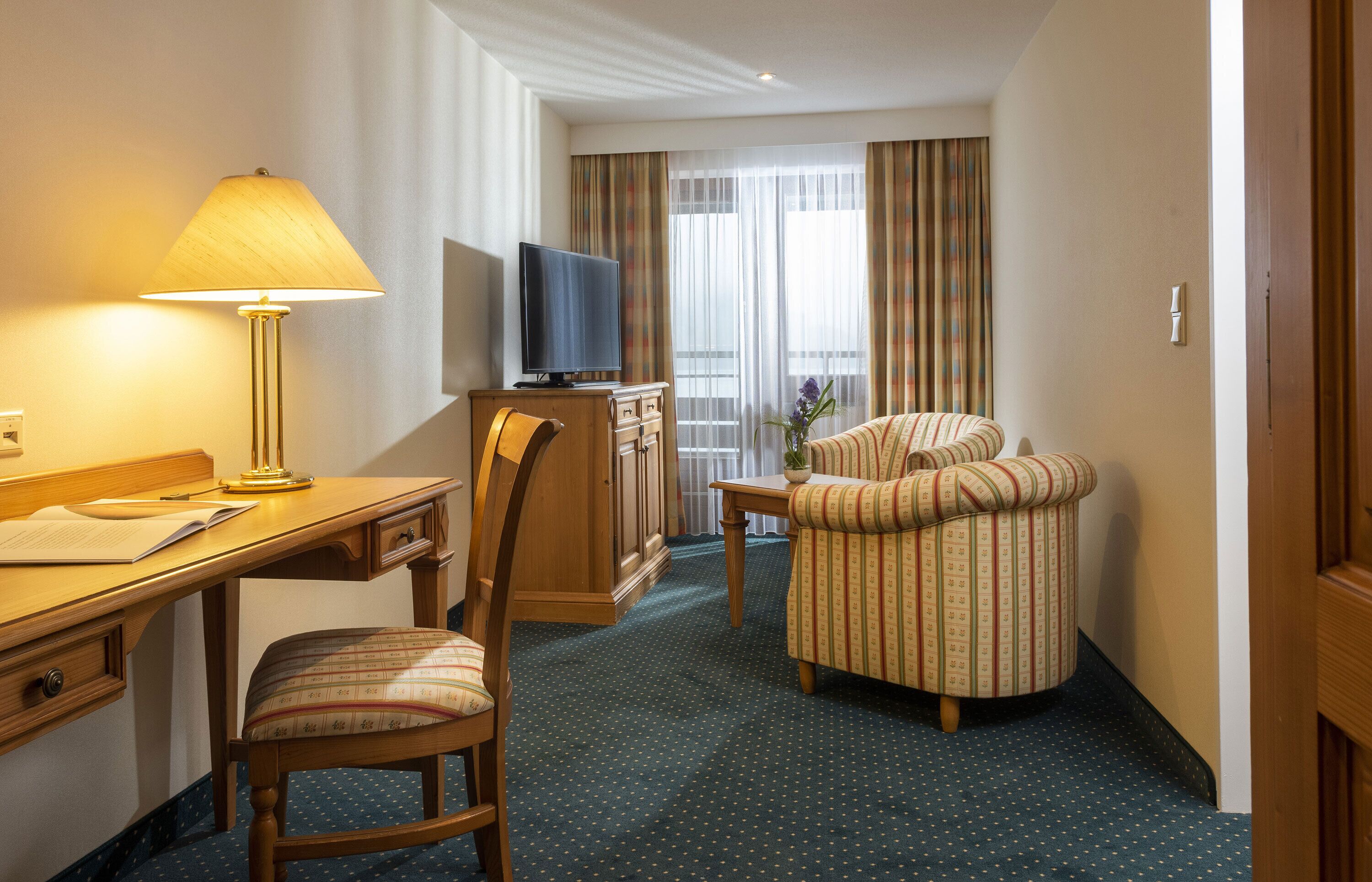 Quarto de hotel com escrivaninha, cadeira, televisão e vista para o exterior pela janela.