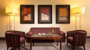Quarto de hotel com carpete estampado, sofá, duas poltronas, mesa de centro e três quadros na parede.